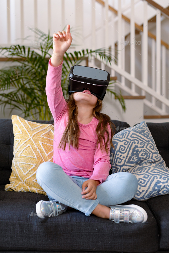 Happy caucasian girl sitting on sofa, wearing vr headset, having fun ...