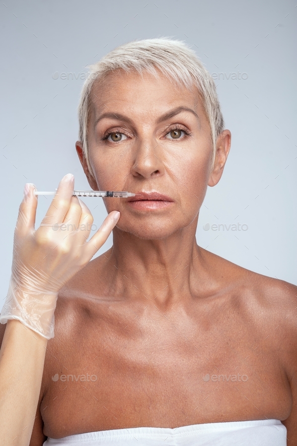 Serious blonde female person doing pick into lips Stock Photo by Iakobchuk