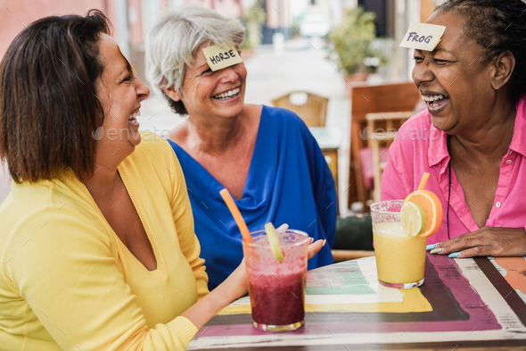 Multiracial senior women having fun playing guessing forehead game at ...