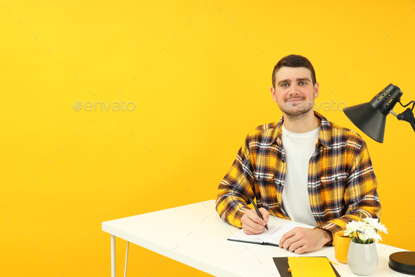 Study concept with young man sitting on the table on yellow background ...