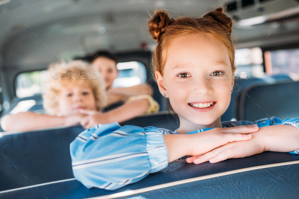 close-up portrait of smiling little schoolgirl riding on school bus ...