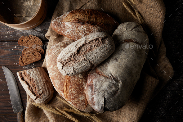 top view of various types of bread, wheat, knife, sieve and sackcloth ...