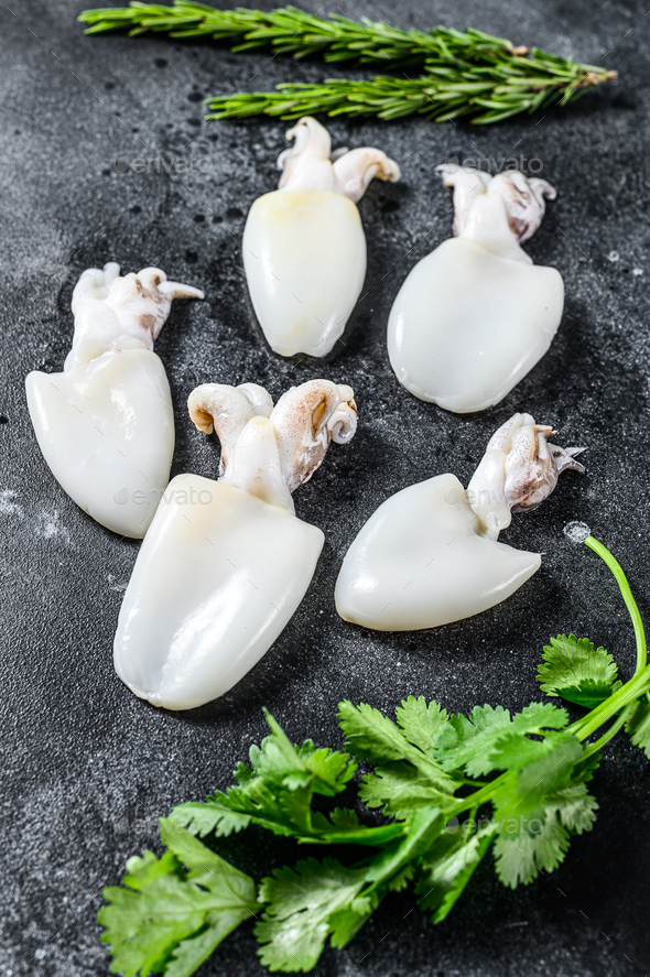 raw mini cuttlefish with rosemary and parsley. Black background. Top ...
