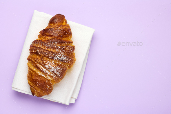 Freshly baked croissant with sugar powder on a purple background with ...