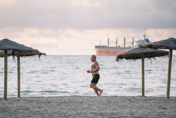 Strong old man makes exercise on the beach. Stock Photo by ADDICTIVE_STOCK