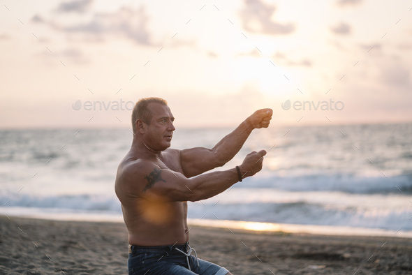 Strong old man makes exercise on the beach. Stock Photo by ADDICTIVE_STOCK