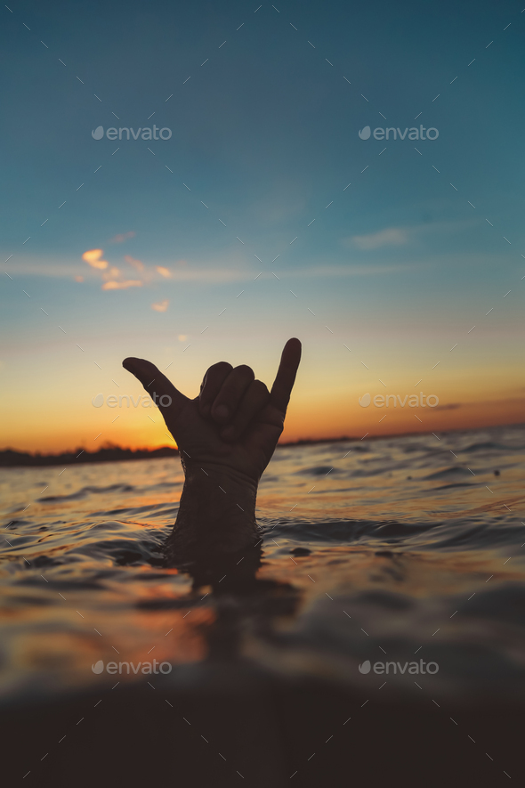 Hand with shaka gesture between water surface and sky at sunset Stock ...