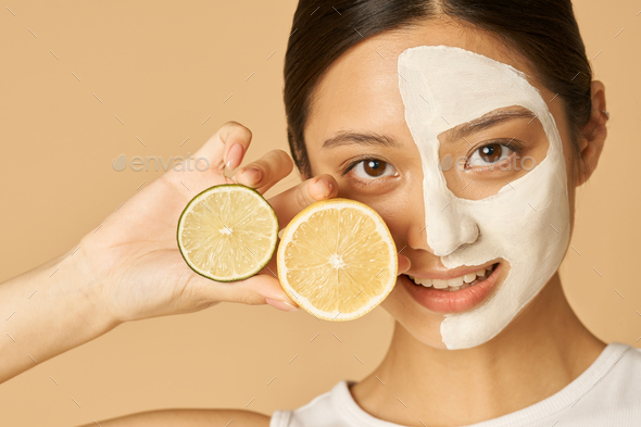 Young woman with facial mask applied on half of her face holding slice ...