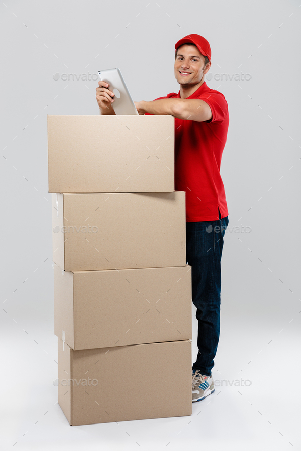 Young delivery man using tablet-computer while posing with boxes Stock ...