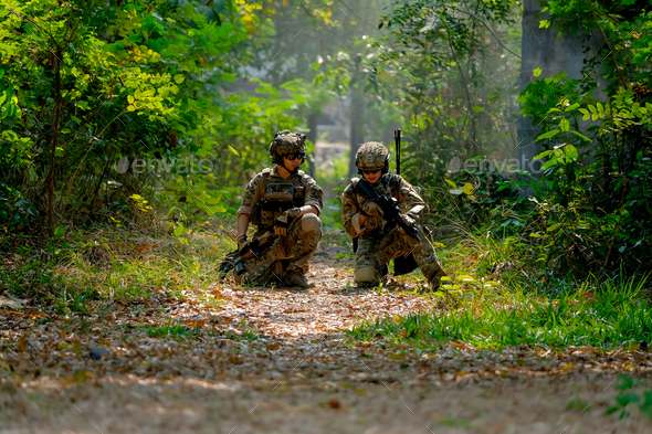 Two soldiers with the fighting uniform sit on the ground and discuss ...