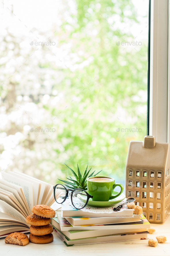 Coffee cup, open book, glasses, cookies and flower on window with bokeh ...