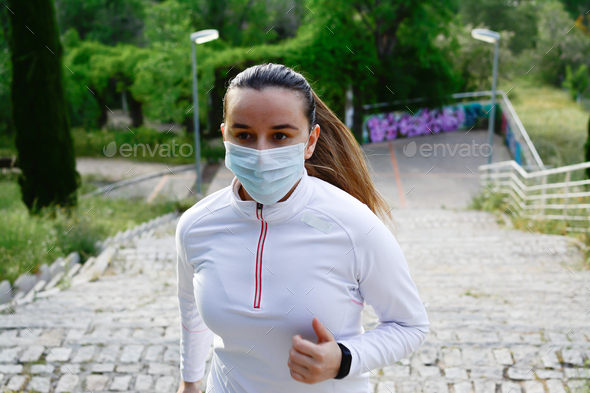 Athletic blonde woman with a mask on her face and a ponytail running in ...
