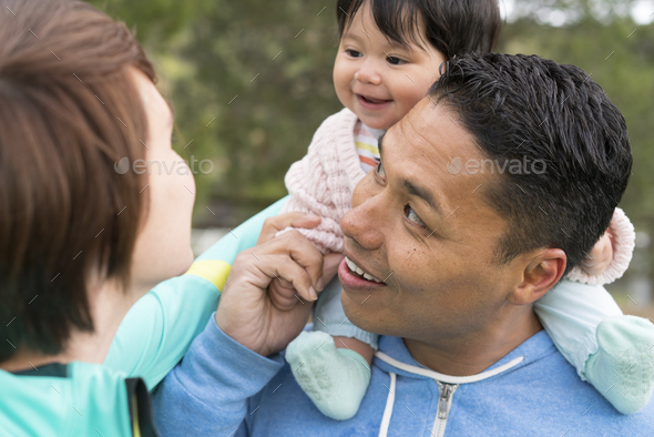 Couple playing piggyback ride with baby in park Stock Photo by nualaimages