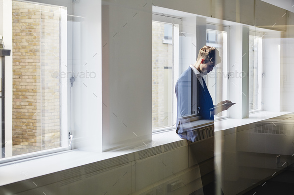 View through glass of man leaning against windowsill looking down at ...