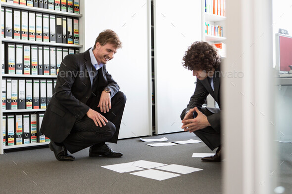 Businessmen laying paperwork on office floor Stock Photo by nualaimages