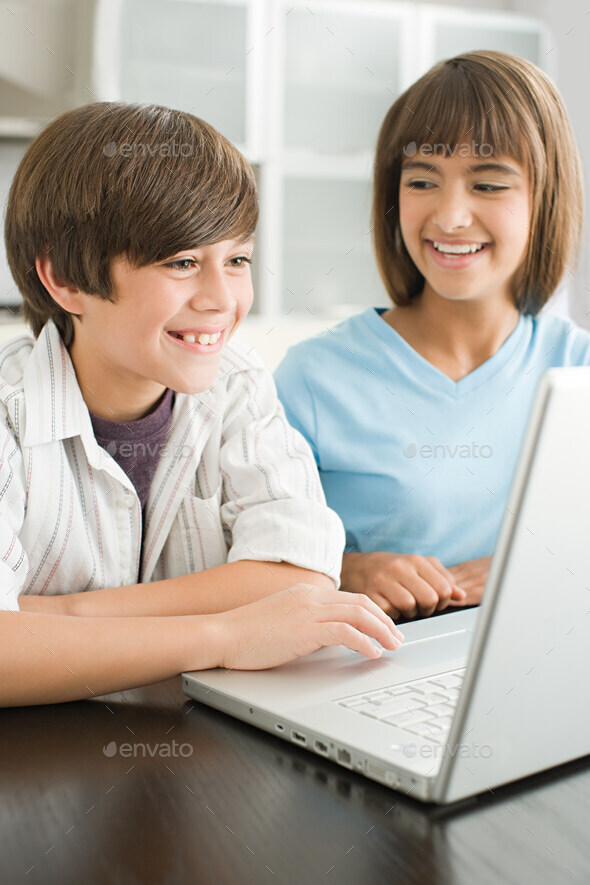 Brother and sister using a laptop computer Stock Photo by nualaimages