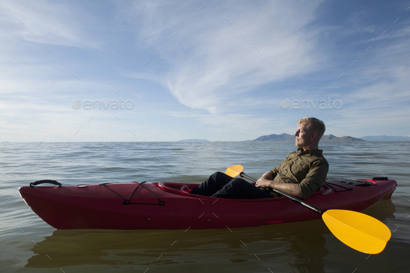 Side view of young man in kayak on water holding paddles, eyes closed ...