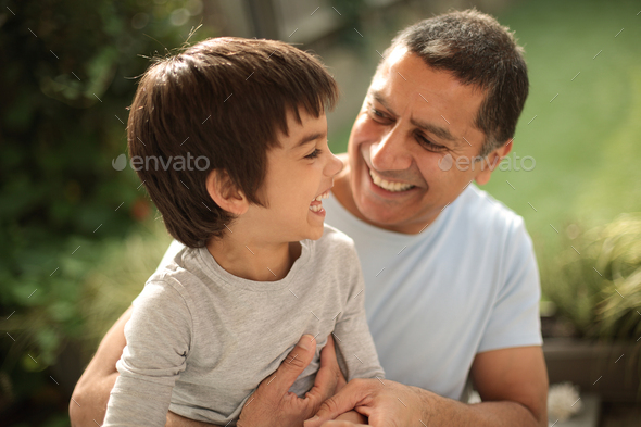 Boy sitting on father's lap, face to face laughing Stock Photo by ...