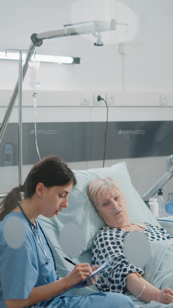 Medical assistant doing checkup visit for patient in hospital ward bed ...