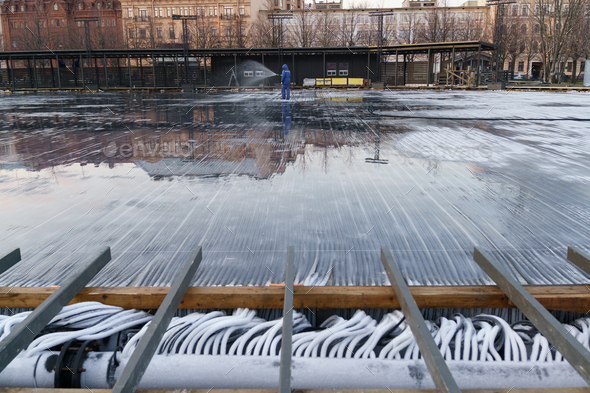 Filling ice rink with water: workman holding hose pouring water on ...