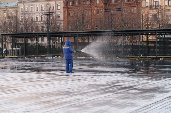 Man worker leveling with water ice rink for hockey or outdoor skating ...