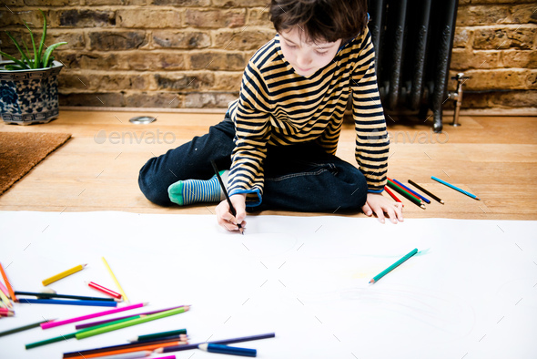 Boy sitting on floor drawing on large paper Stock Photo by Image-Source