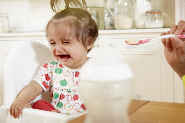 Baby girl crying while being fed breakfast by mother Stock Photo by ...