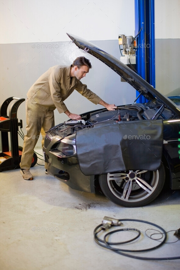 Mechanic working on car engine in garage Stock Photo by Image-Source