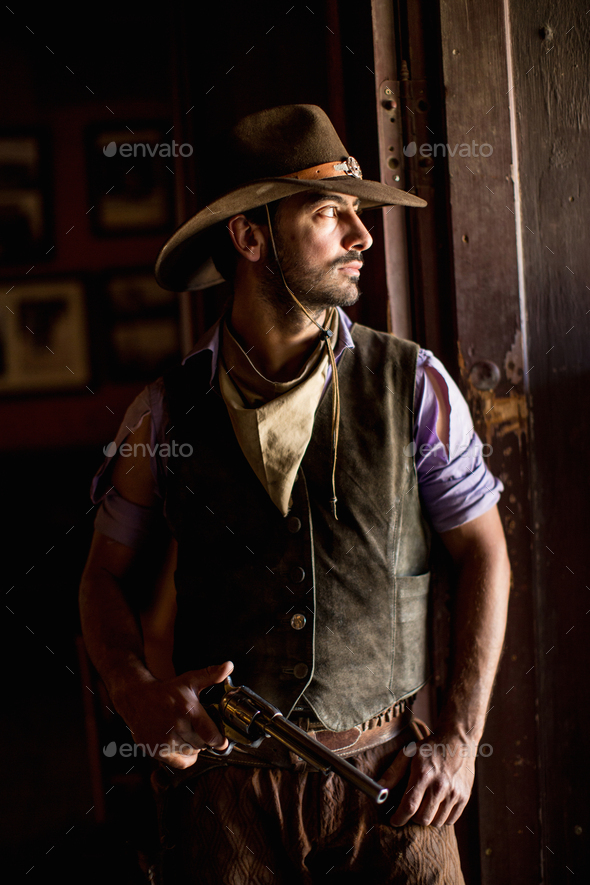 Portrait of cowboy holding handgun in doorway on wild west film set ...