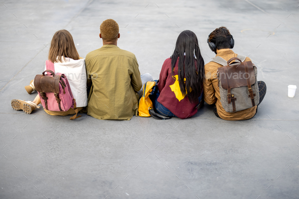 Back view of students sit and rest on asphalt Stock Photo by RossHelen