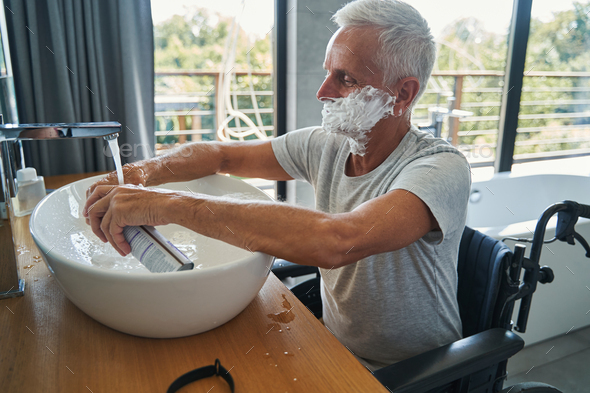 Male wheelchair user washing hands after applying shaving cream Stock ...