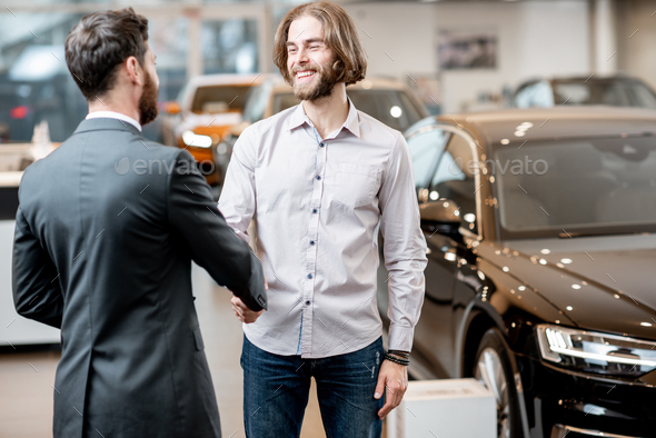 Salesperson with client in the car showroom Stock Photo by RossHelen