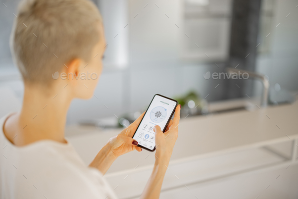 Girl using app of smart home on smartphone Stock Photo by RossHelen