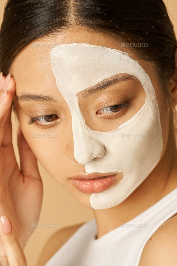 Close up shot of young woman with facial mask applied on half of her ...
