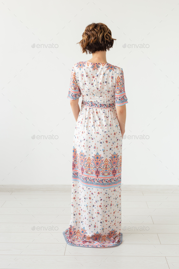Rear view of a young slim woman in a long patterned dress standing ...