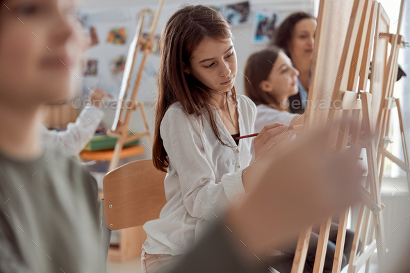 Young creative happy pupils at light modern classroom are doing drawing ...
