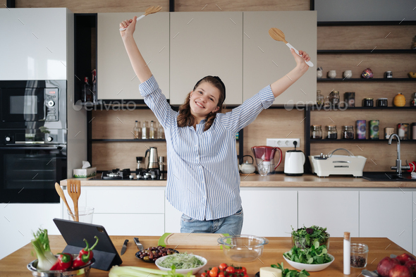 Cheerful girl dancing while cooking holding hands up Stock Photo by diignat