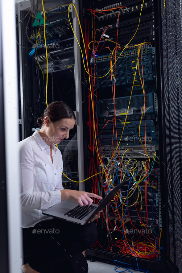 Caucasian female engineer with laptop inspecting computer server in ...
