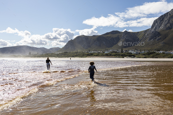 Teenage girl and a boy running through shallow water on a wide sandy ...