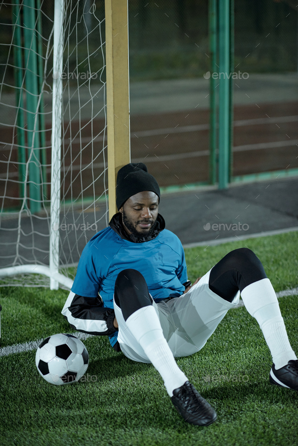 Tired football player in professional sports uniform sitting by net ...