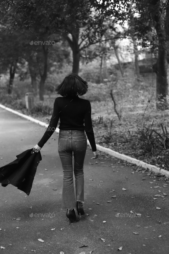 Back view of woman walking on pathway between trees in grayscale Stock ...