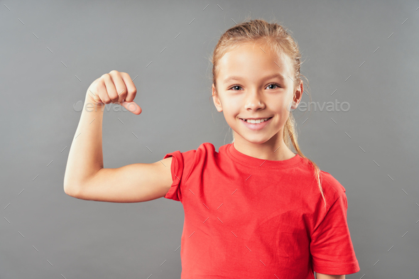 Adorable girl in red shirt demonstrating biceps muscle Stock Photo by ...