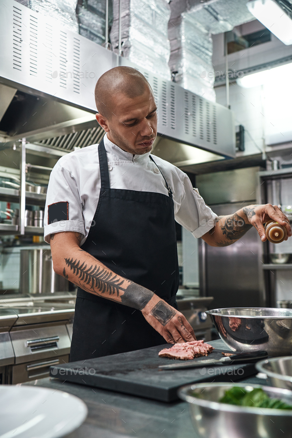 Last details. Serious bald chef in apron and with beautiful tattoos on ...