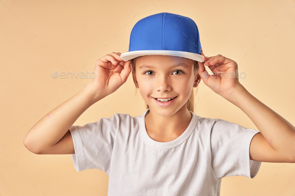 Adorable joyful girl putting on blue baseball cap Stock Photo by ...