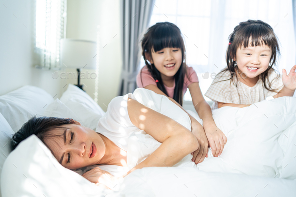 Asian happy children jumping on bed to waking up mother in the morning ...