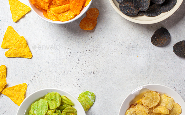 Frame of different types of colored potato chips in white bowls, gray ...