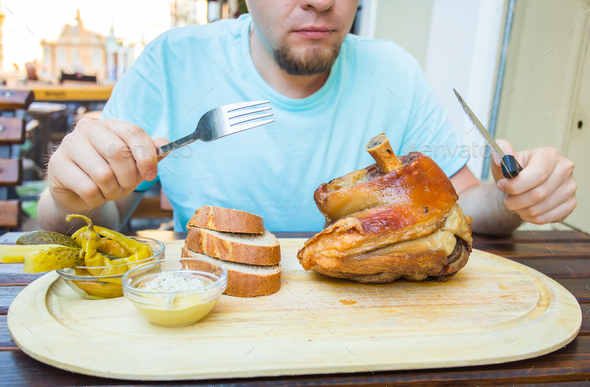 man eating knuckle of pork and drinks beer close-up Stock Photo by Satura_