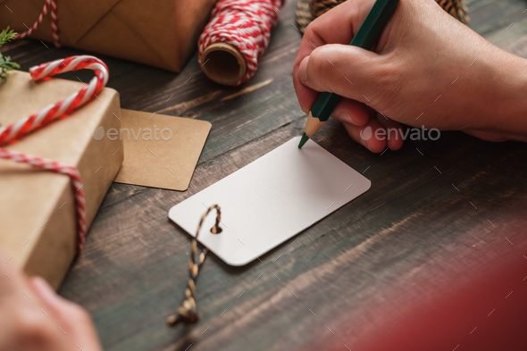 woman writing gift tag and attach to christmas present on wood table ...