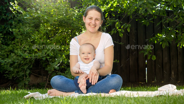 Cute baby boy sitting on mothers lap in park and smiling in camera ...