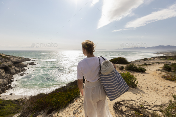 Teenage girl standing on top of a cliff looking over the coastline and ...